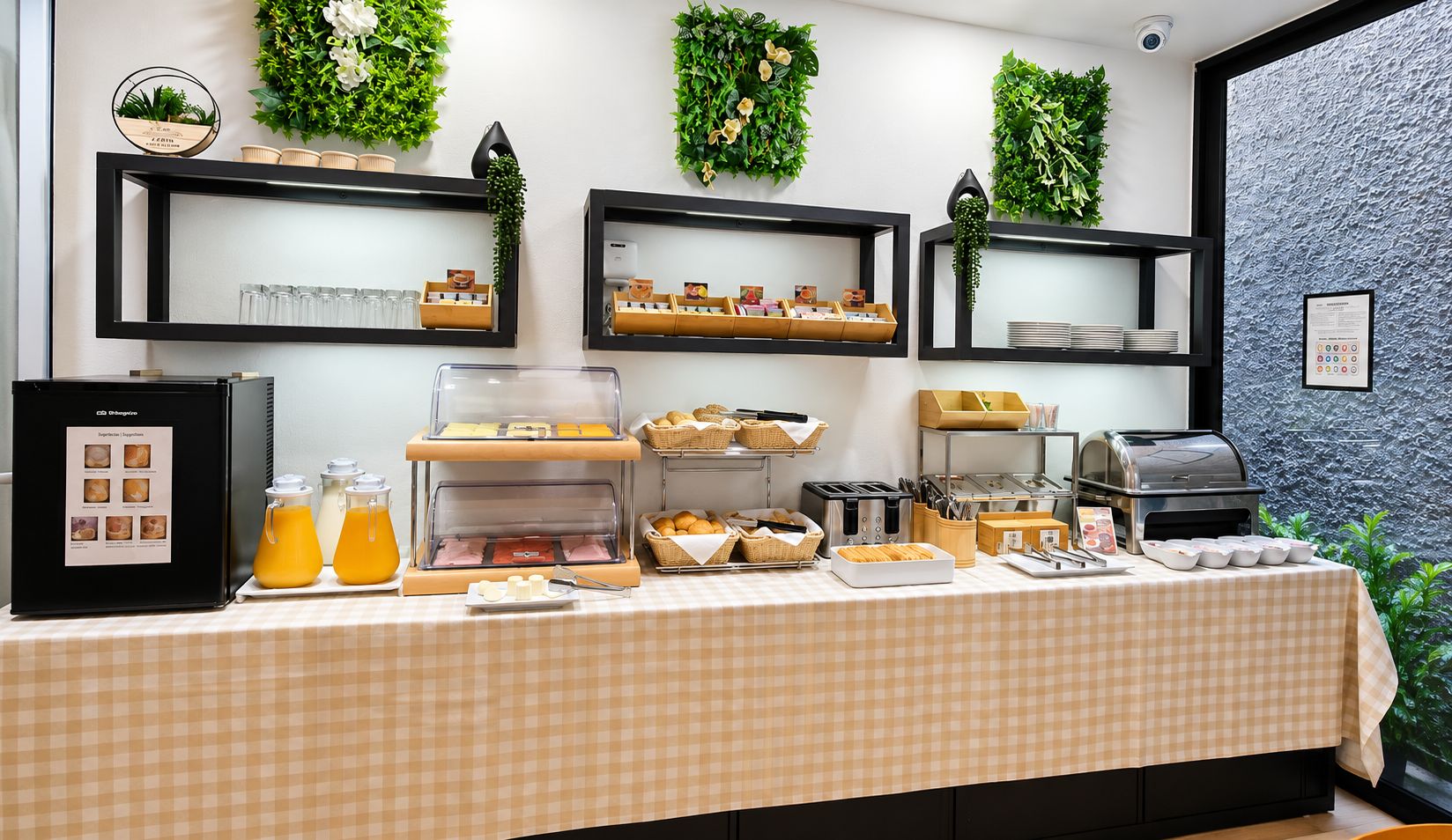 Disposição de buffet com diversos alimentos e um canto de café, rodeado por plantas decorativas nas paredes e quadros emoldurados.