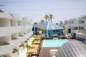 Uma área de piscina no terraço, com estrutura de vidro, espreguiçadeiras e vista clara dos edifícios ao redor.