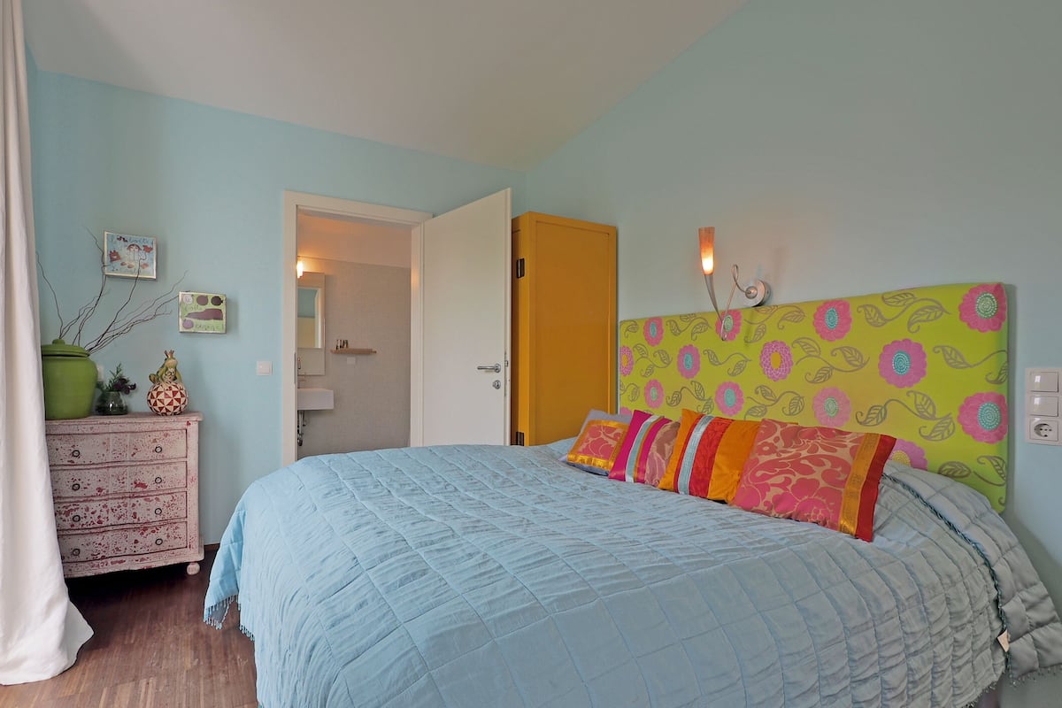Quarto com cama, cômoda e porta que dá para outro espaço.
