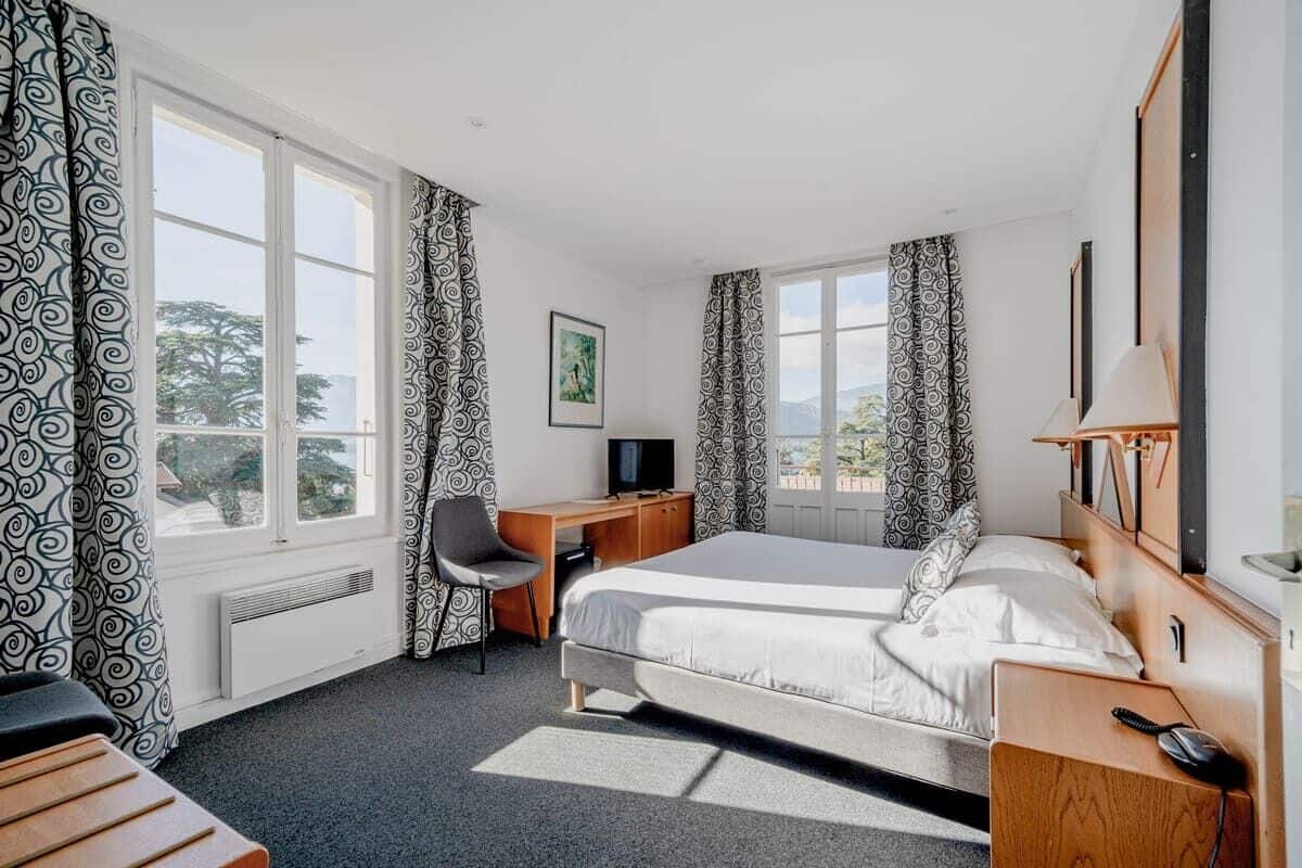 Quarto de hotel com uma cama grande, uma escrivaninha, uma cadeira e uma televisão.