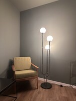 Quarto moderno com piso de madeira, uma poltrona verde e um abajur com três luminárias esféricas.