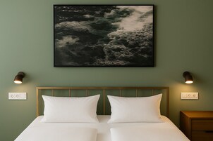 Quarto com cama, duas luminárias laterais e um quadro na parede.