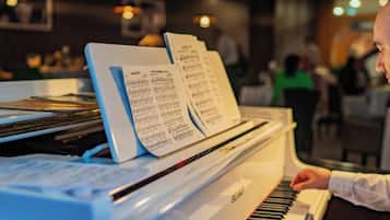 Um piano com partituras, em uma sala com mesas e cadeiras.