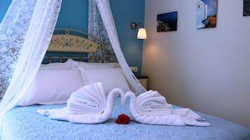 Uma cama com dossel, uma rosa vermelha e duas toalhas em forma de cisne.
