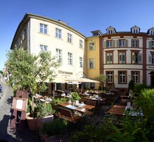 Restaurante com mesas ao ar livre, fachada de prédio curva e céu azul.