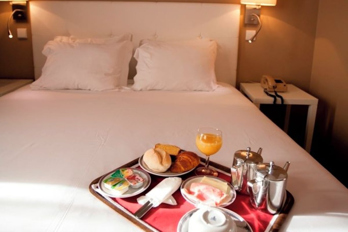 Quarto de hotel com cama bem arrumada, bandeja com itens de café da manhã e abajures.
