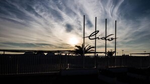 Vista do pôr do sol com cerca e palmeiras, e a palavra 'Cicco' escrita numa estrutura.