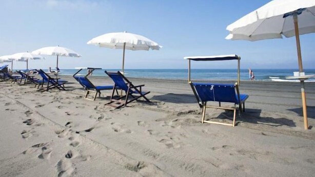Uma praia com fileiras de cadeiras-de-sol azuis e guarda-sóis brancos.