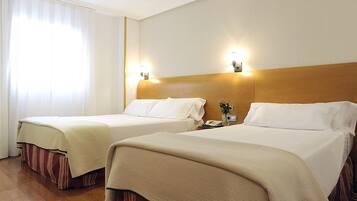 Quarto de hotel com duas camas, cada uma com cabeceira de madeira, roupa de cama branca e mesa de cabeceira com luminária.