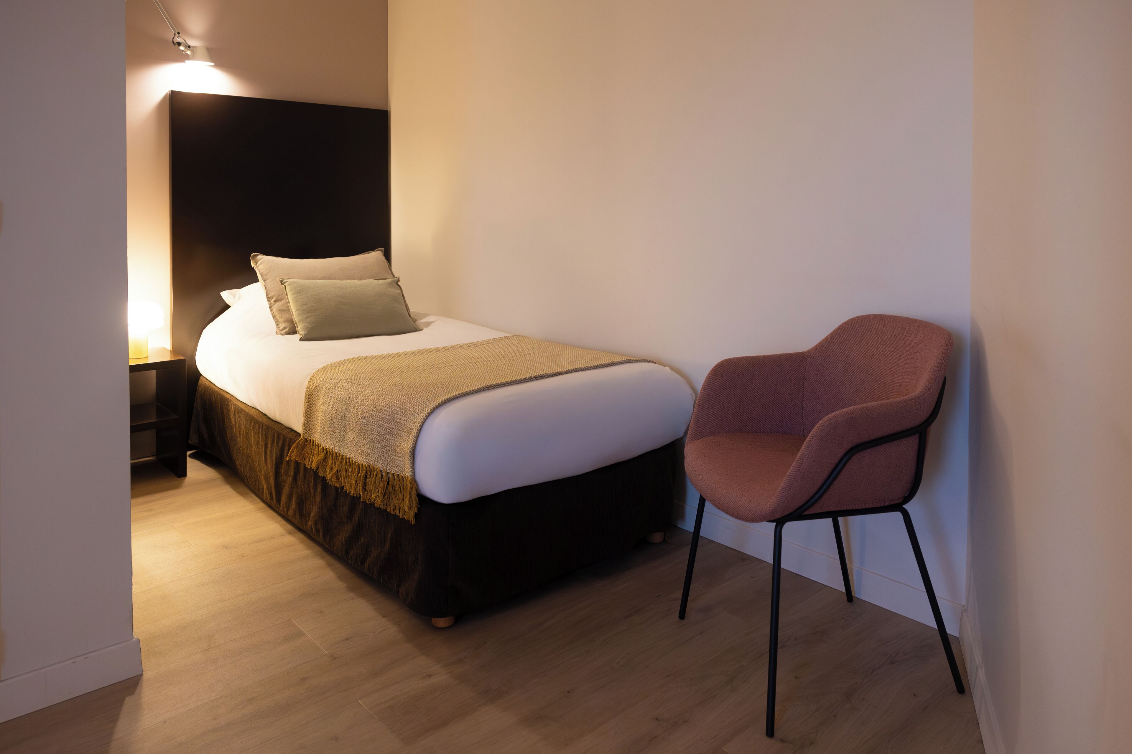Quarto com uma cama, uma cadeira e uma mesa de cabeceira com abajur.