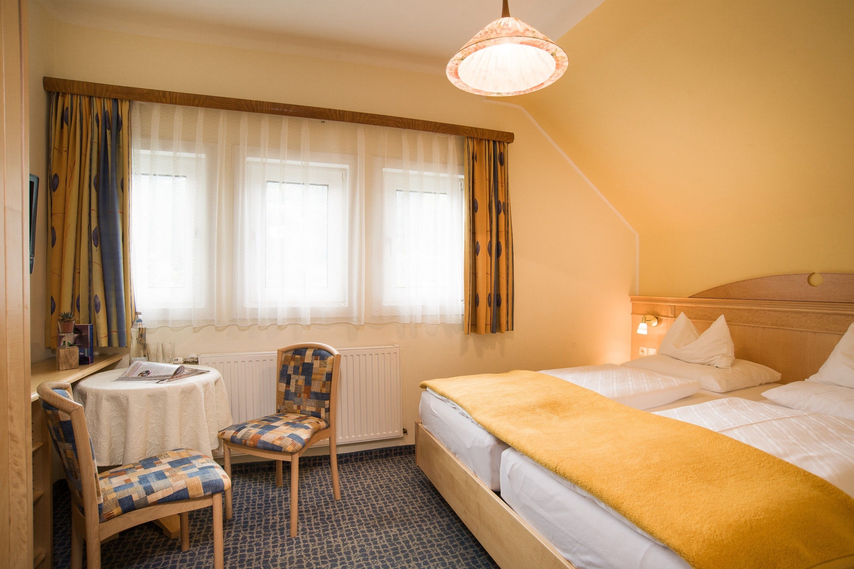 Quarto de hotel com cama, cadeira, mesa e janela com cortinas.