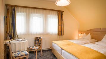 Quarto de hotel com cama, cadeira, mesa e janela com cortinas.