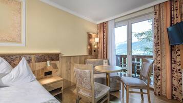 Quarto de hotel com cama, escrivaninha, cadeira, mesa pequena e varanda com vista para as montanhas.