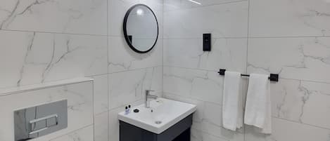 Um banheiro moderno com piso de mármore, espelho redondo, pia branca e vaso sanitário.
