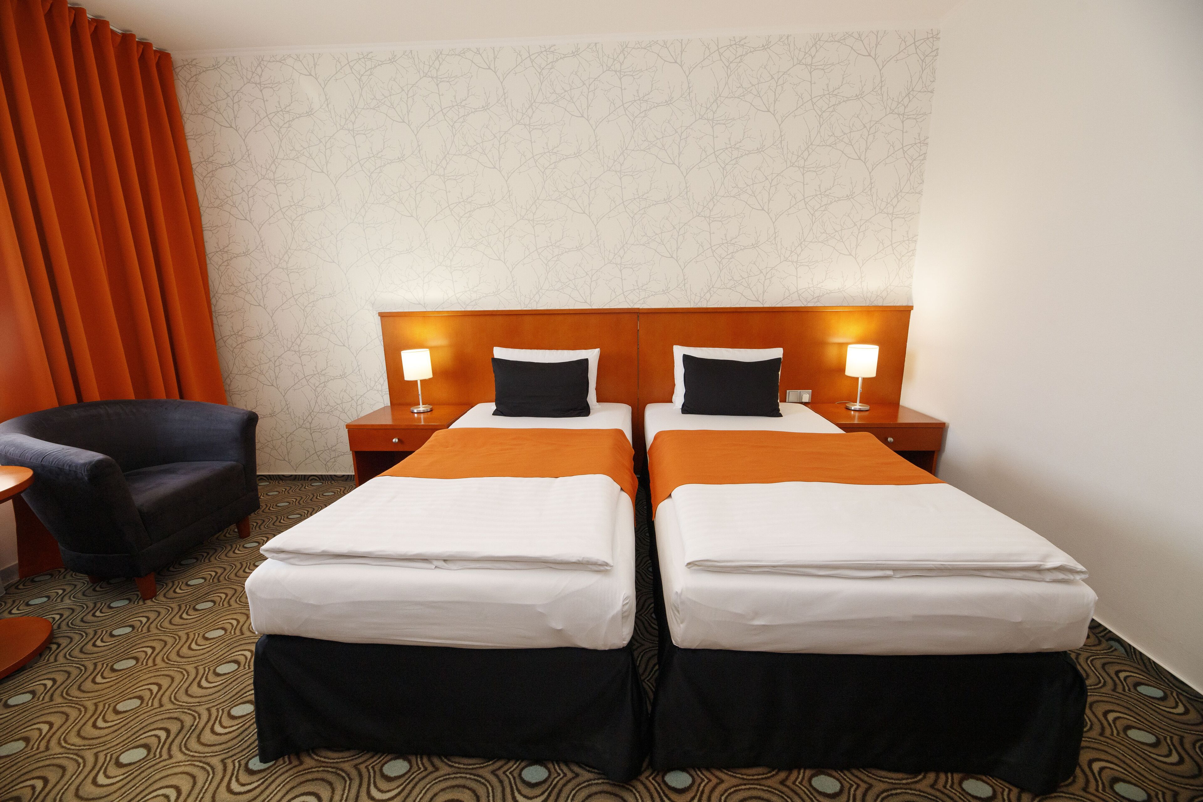 Quarto de hotel com duas camas, uma cadeira e um tapete estampado.