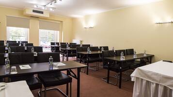 Sala de conferências com várias mesas e cadeiras, equipada com garrafas de água e canetas.