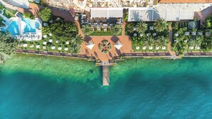 Vista aérea de um resort com piscina central, um píer e palmeiras ao redor.