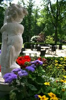 Estátua de mulher num jardim, com mesas e cadeiras ao fundo.