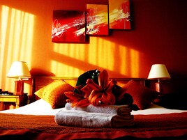 Quarto de hotel com uma cama, duas luminárias de cabeceira, um arranjo floral decorativo e três obras de arte nas paredes.
