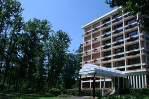 Um hotel com vários andares e entrada coberta, rodeado por vegetação exuberante e árvores.