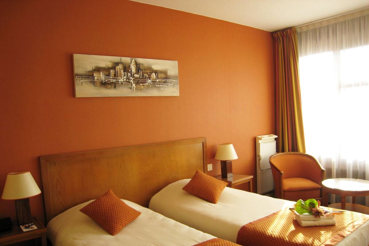 Quarto de hotel com duas camas, um quadro na parede, uma cadeira, uma mesa e um abajur.