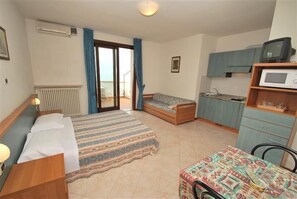 Quarto com cama, sofá, mesinha, cozinha compacta e vista através de uma porta de vidro.
