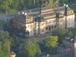 Um edifício grande e histórico com várias alas e um pátio central, rodeado por árvores.