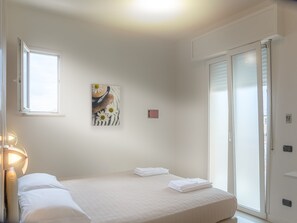 Quarto de hotel com cama, um quadro, uma janela e uma porta.
