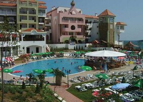 Um hotel com piscina rodeada por espreguiçadeiras e guarda-sóis, um jardim ajardinado e edifícios com várias plantas com varandas.