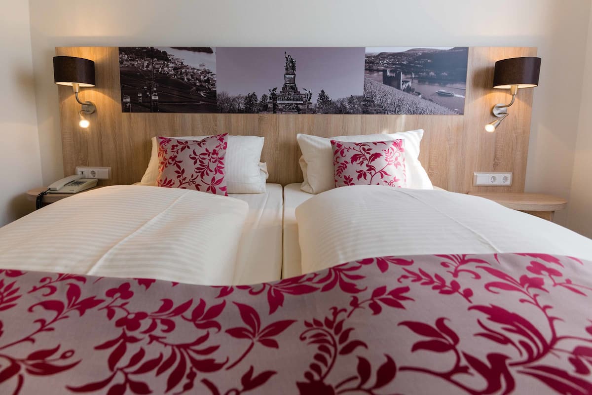 Quarto de hotel com duas camas, uma mesa de cabeceira com telefone e uma luminária fixada na parede.