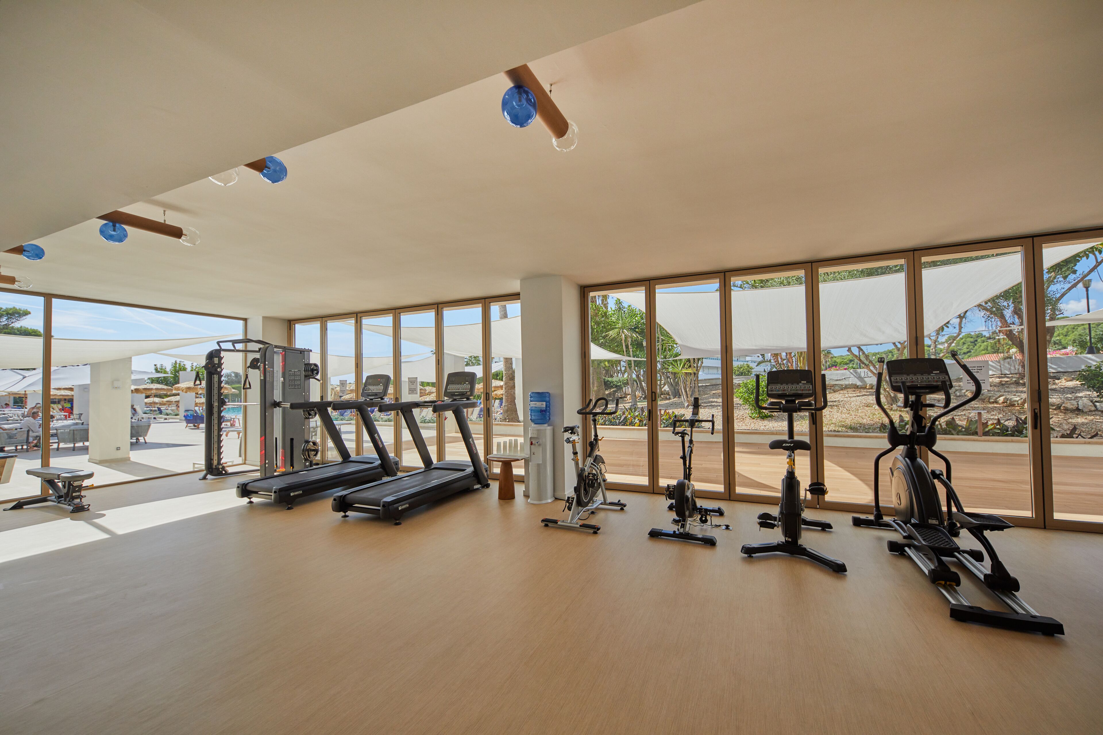 Uma academia ampla com diversos equipamentos de exercícios, grandes janelas e vista para o exterior.