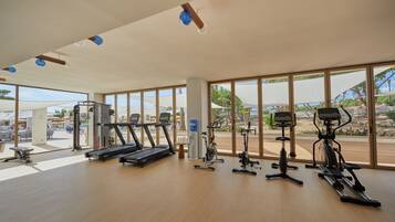 Uma academia ampla com diversos equipamentos de exercícios, grandes janelas e vista para o exterior.