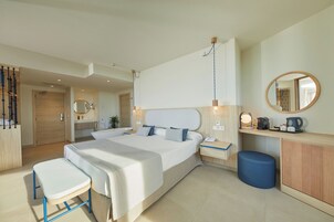Quarto de hotel moderno com uma cama grande, mesas de cabeceira, escrivaninha, cadeira, espelho e um banquinho azul.