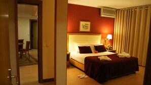 Quarto de hotel com uma cama, mesa de cabeceira, abajur e um quadro na parede.