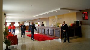 Um lobby de hotel com uma mesa de recepção, um tapete vermelho e uma placa com a inscrição "PALACE HOTEL & SPA MONTERIO".