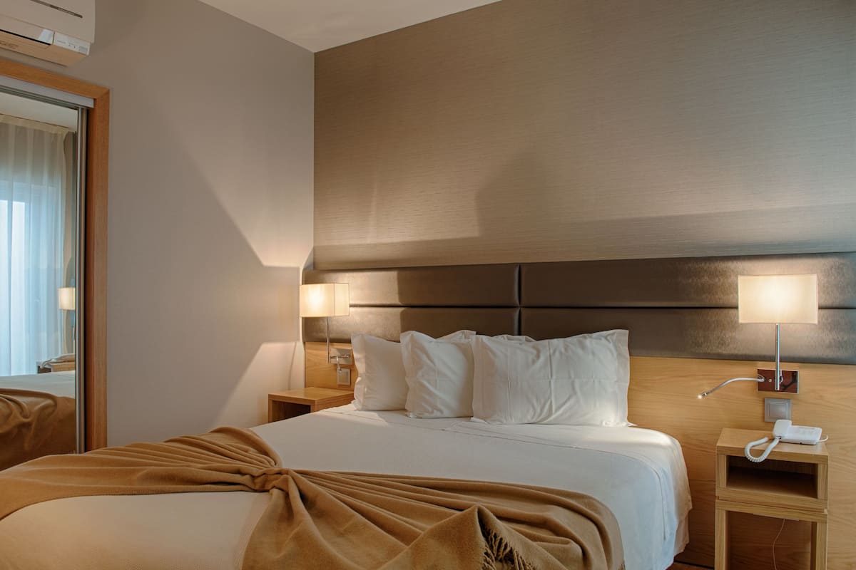 Quarto de hotel com uma cama grande, duas mesas de cabeceira, um abajur, um telefone e um espelho.