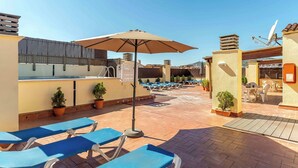Terraço no telhado com cadeiras de estar azuis, um grande guarda-sol e vasos de plantas.