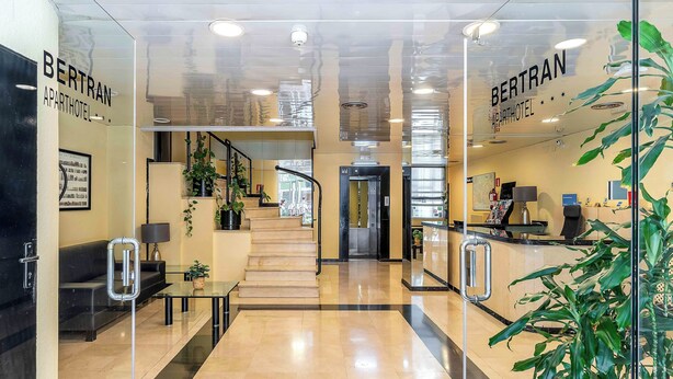 Um saguão moderno de hotel com balcão de recepção, área de estar e escadas que levam aos andares superiores.