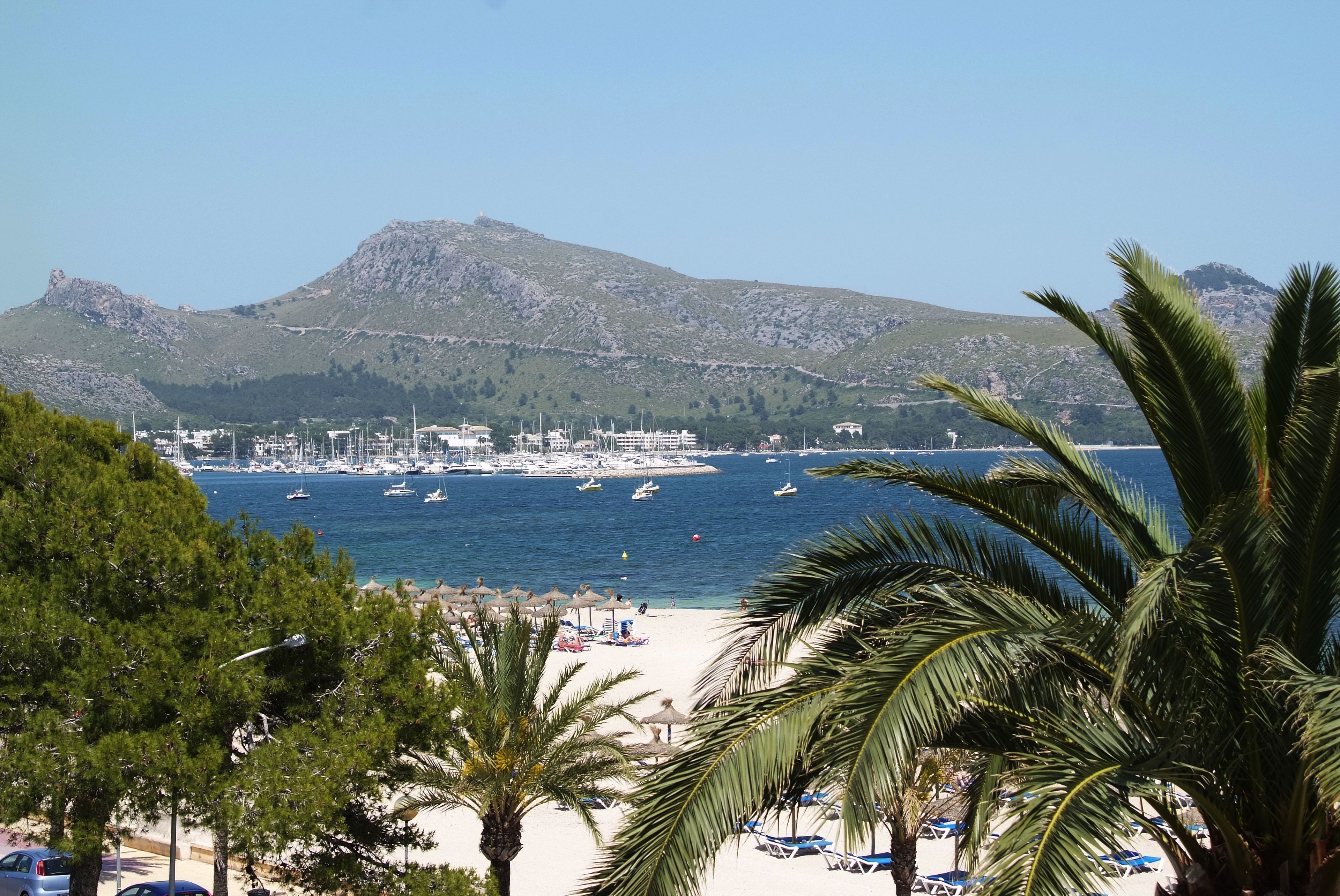 Vista costeira com praia, barcos e montanhas ao fundo.