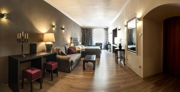 Quarto de hotel moderno com sofá, duas poltronas, mesa de centro, escrivaninha com luminária e espelho.