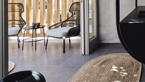 Um interior moderno com uma divisória de madeira, duas cadeiras pretas, uma pequena mesa redonda e um banco preto.