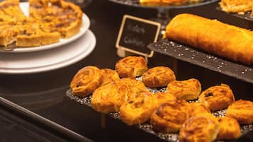 Um buffet com diversos produtos de panificação, incluindo doces, muffins e um grande rolinho de canela.
