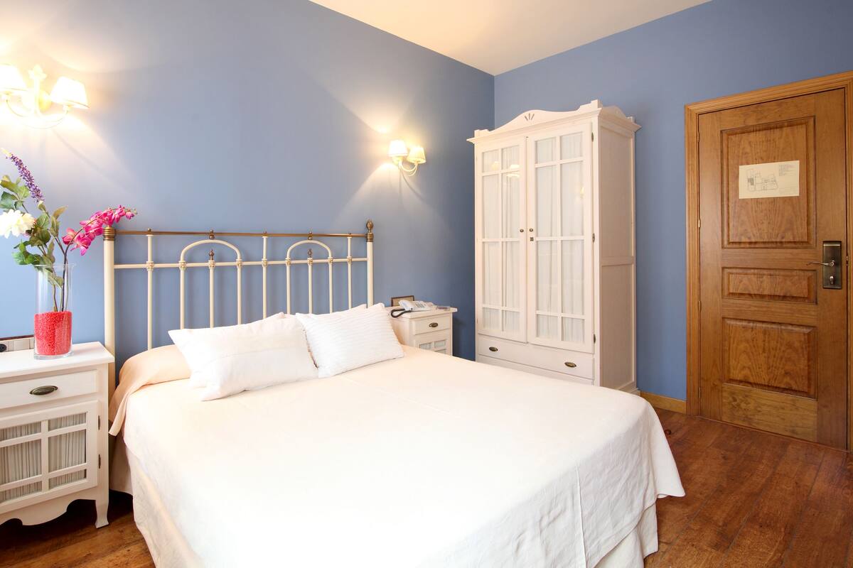 Quarto com cama, mesas de cabeceira, guarda-roupa e porta.