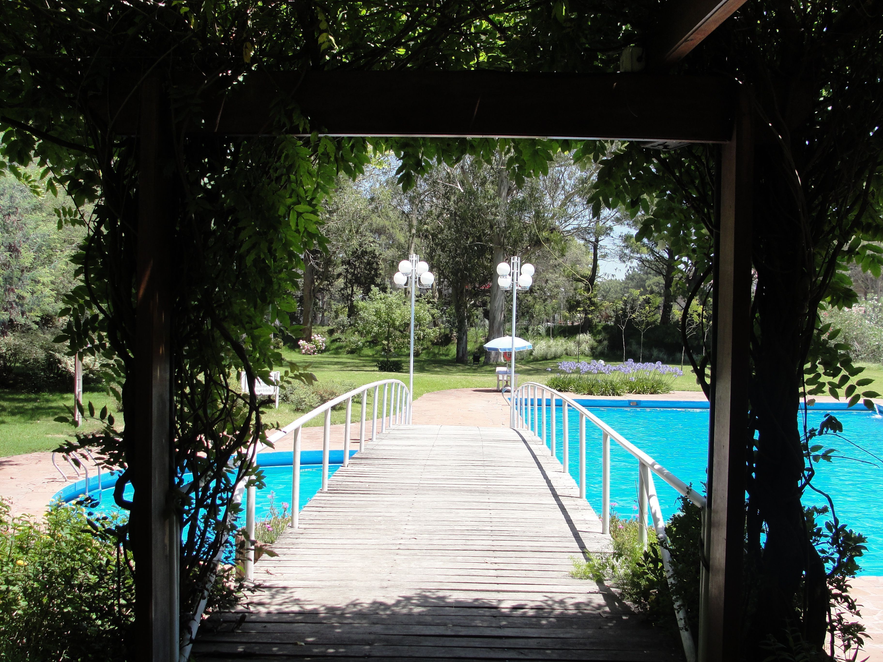 Um deck de madeira que leva a uma piscina com pérgola.