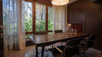 Uma área de refeições com uma mesa comprida, cadeiras e vista para o verde através de grandes janelas.
