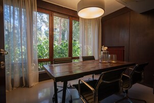 Uma área de refeições com uma mesa comprida, cadeiras e vista para o verde através de grandes janelas.
