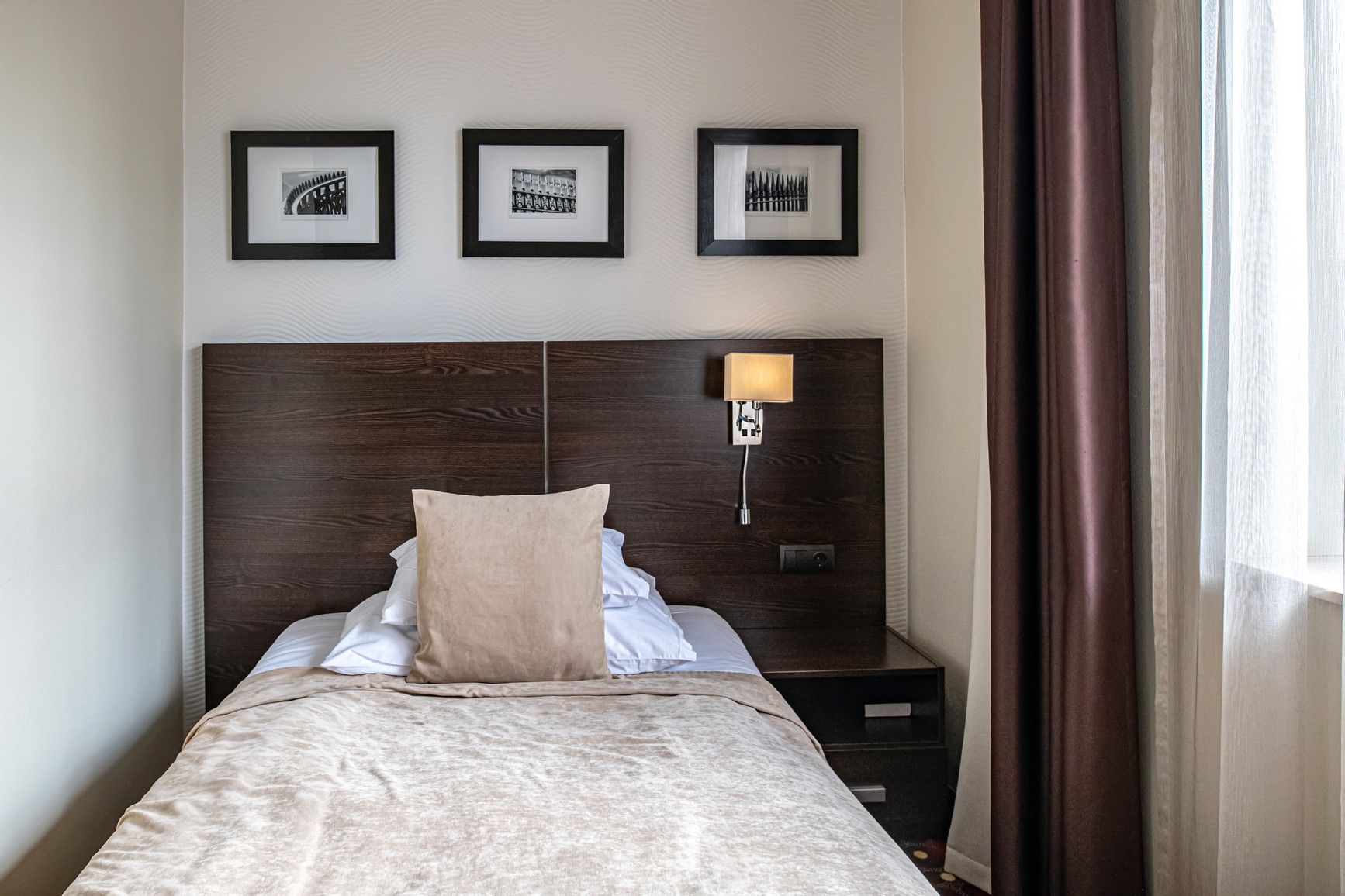 Quarto de hotel com cama, mesa de cabeceira, luminária e três quadros na parede.