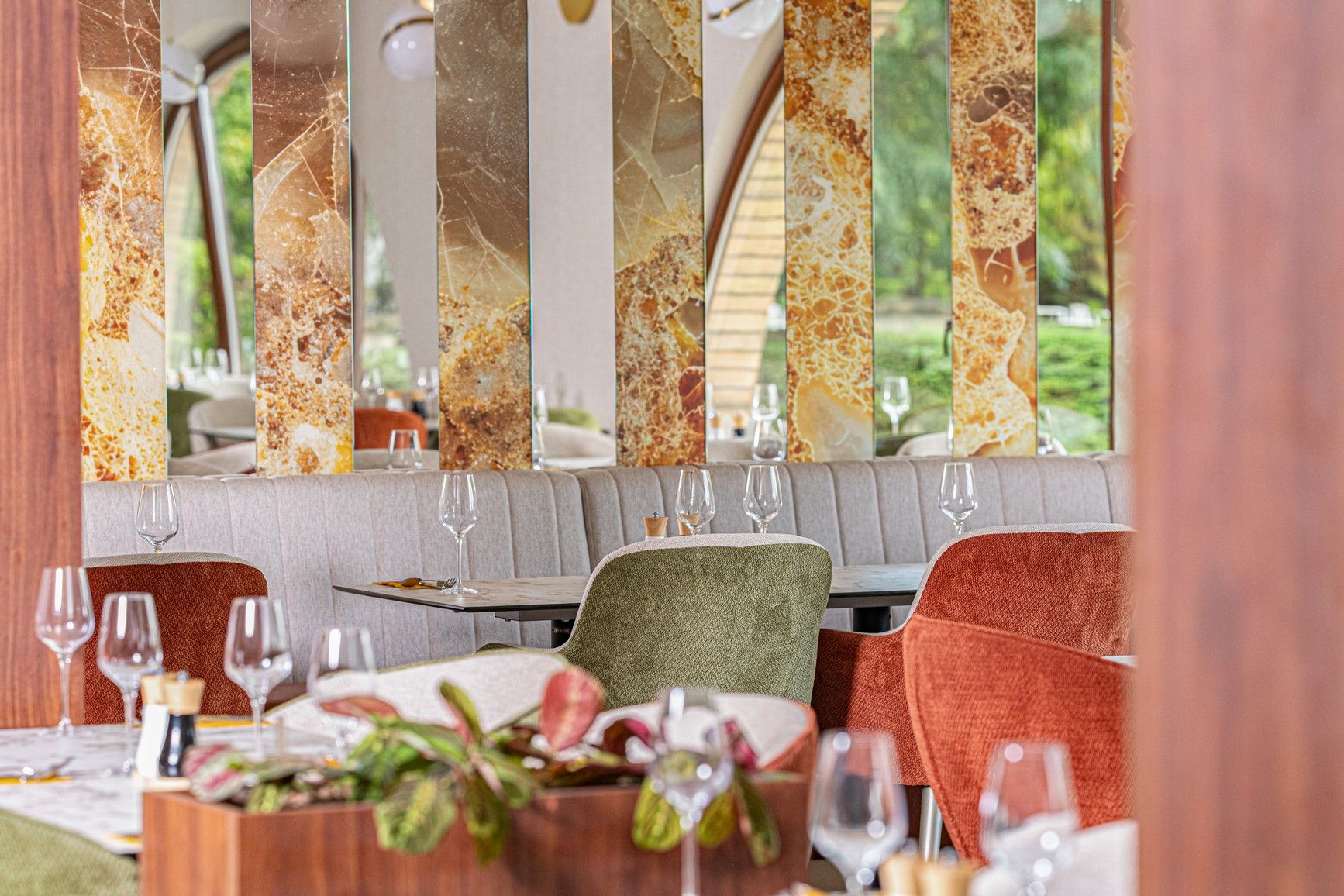 Interior de restaurante com disposição em cabines, uma mesa com um vaso de flores e vista para o verde lá fora.