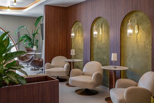 Espaço de convívio moderno com poltronas de couro, mesas redondas e uma grande planta em vaso.