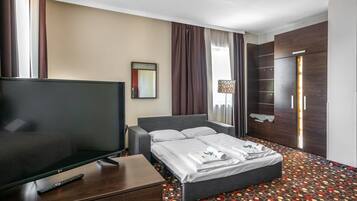 Quarto de hotel com cama, televisão, secretária e guarda-roupa.